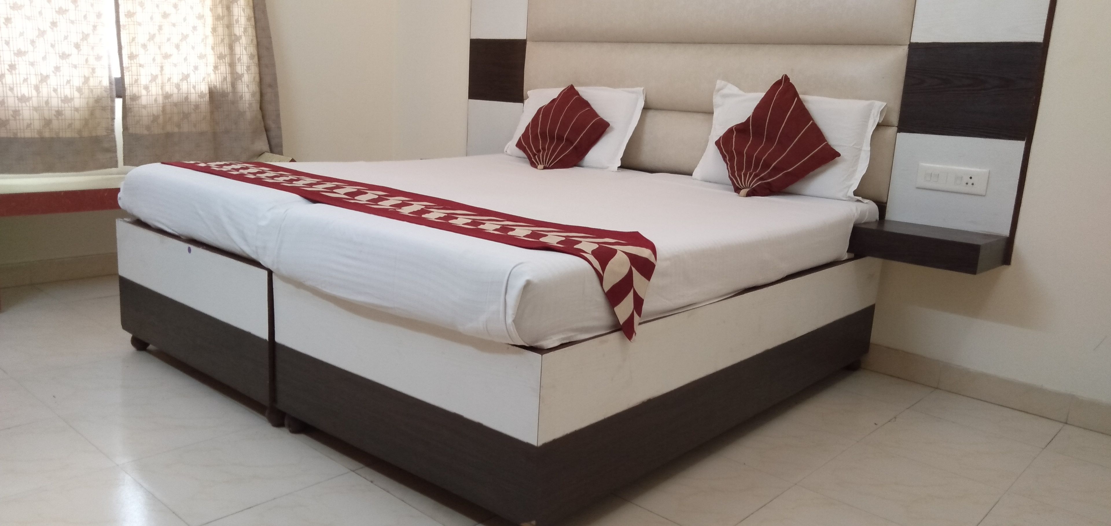 Uma cama bem arrumada com um edredom branco e vermelho, duas almofadas e uma mesa de cabeceira com tomada.