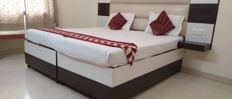 Uma cama bem arrumada com um edredom branco e vermelho, duas almofadas e uma mesa de cabeceira com tomada.