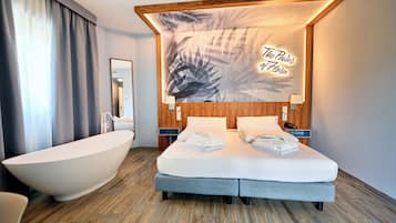 Quarto de hotel moderno com uma banheira grande, cama com duas almofadas e luminária fixada na parede.