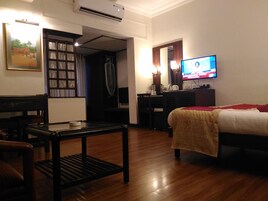 Quarto de hotel com cama, escrivaninha, cadeira, televisão e um quadro na parede.