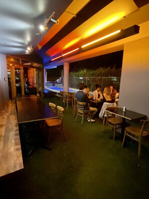 Um espaço de refeições interno com mesas, cadeiras, um balcão de bar e vista para o exterior.