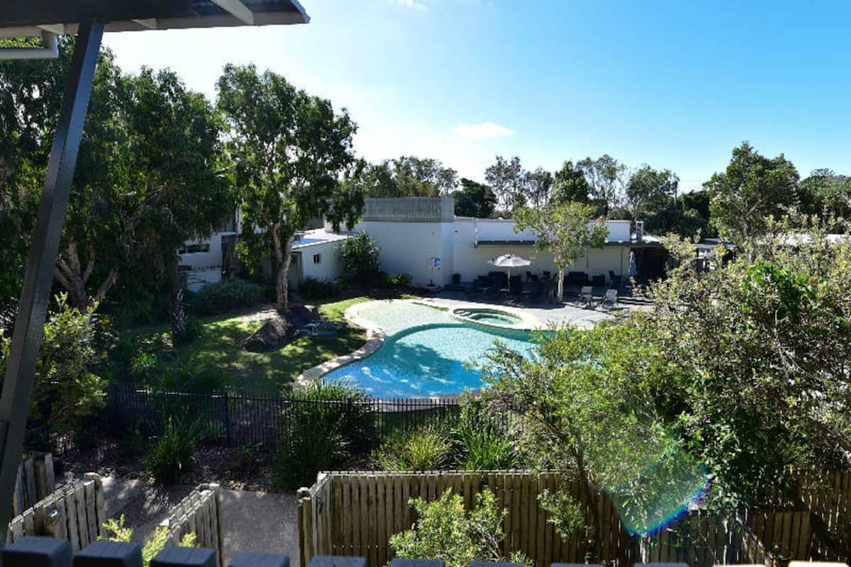 Quintal com piscina, deck de madeira e área cercada com espreguiçadeiras.