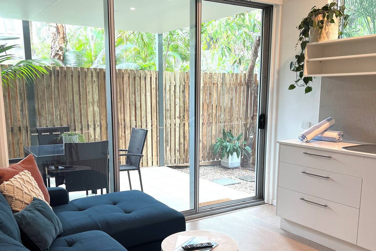 Uma sala de estar moderna com um sofá seccional azul escuro, uma mesa de centro redonda e uma área de jantar com mesa e cadeiras.