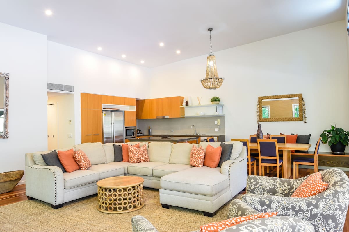 Uma sala de estar moderna com um sofá seccional, uma mesa de centro redonda e uma área de jantar com mesa e cadeiras de madeira.