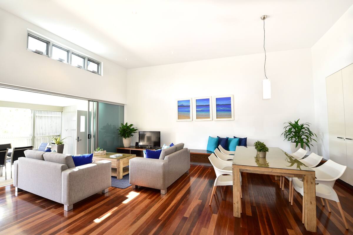 Ampla sala de estar com sofá, mesa de centro e mesa de jantar. Há uma televisão e uma planta na mesa de centro.