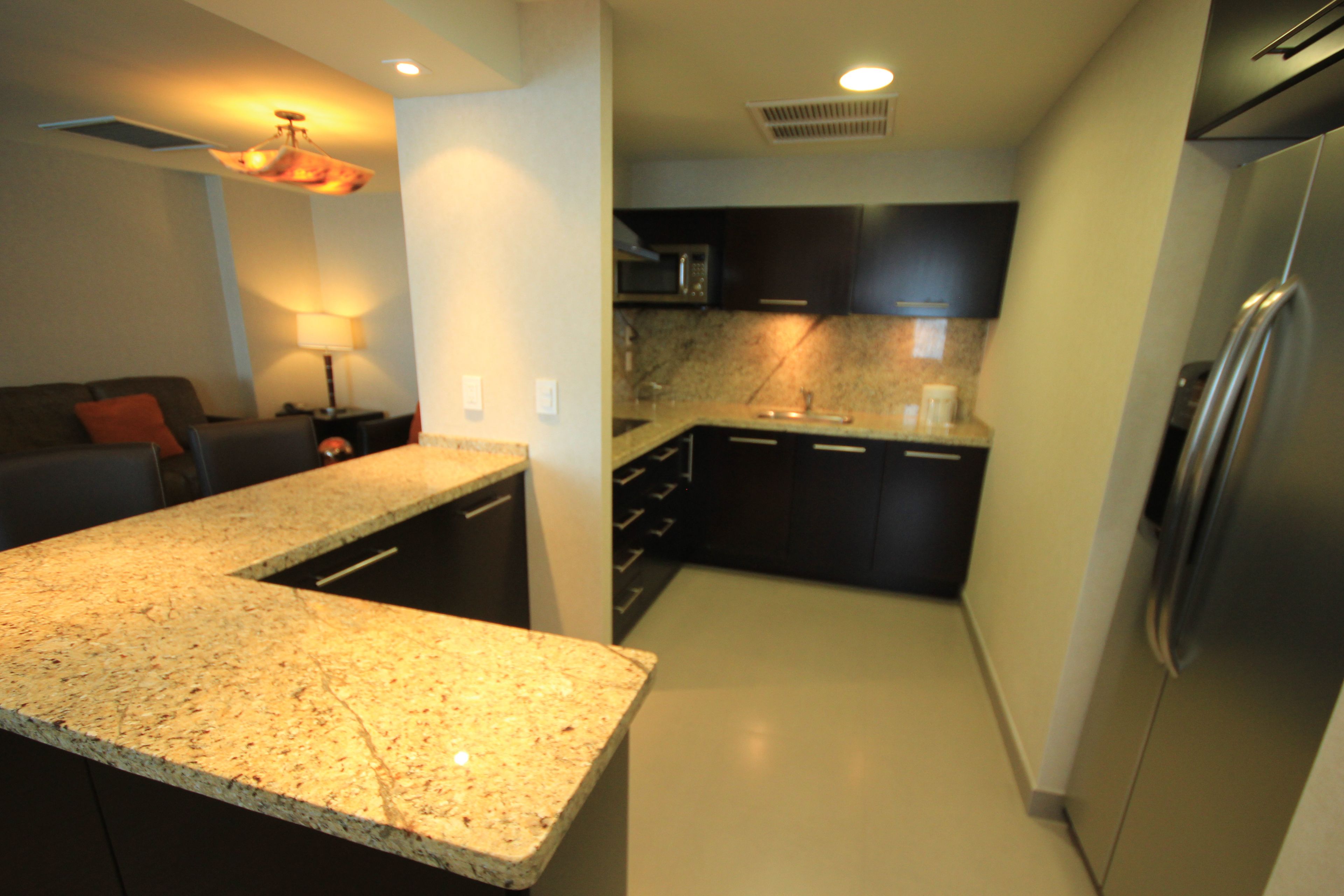 Cozinha moderna com bancadas de granito, armários escuros e eletrodomésticos de aço inoxidável.