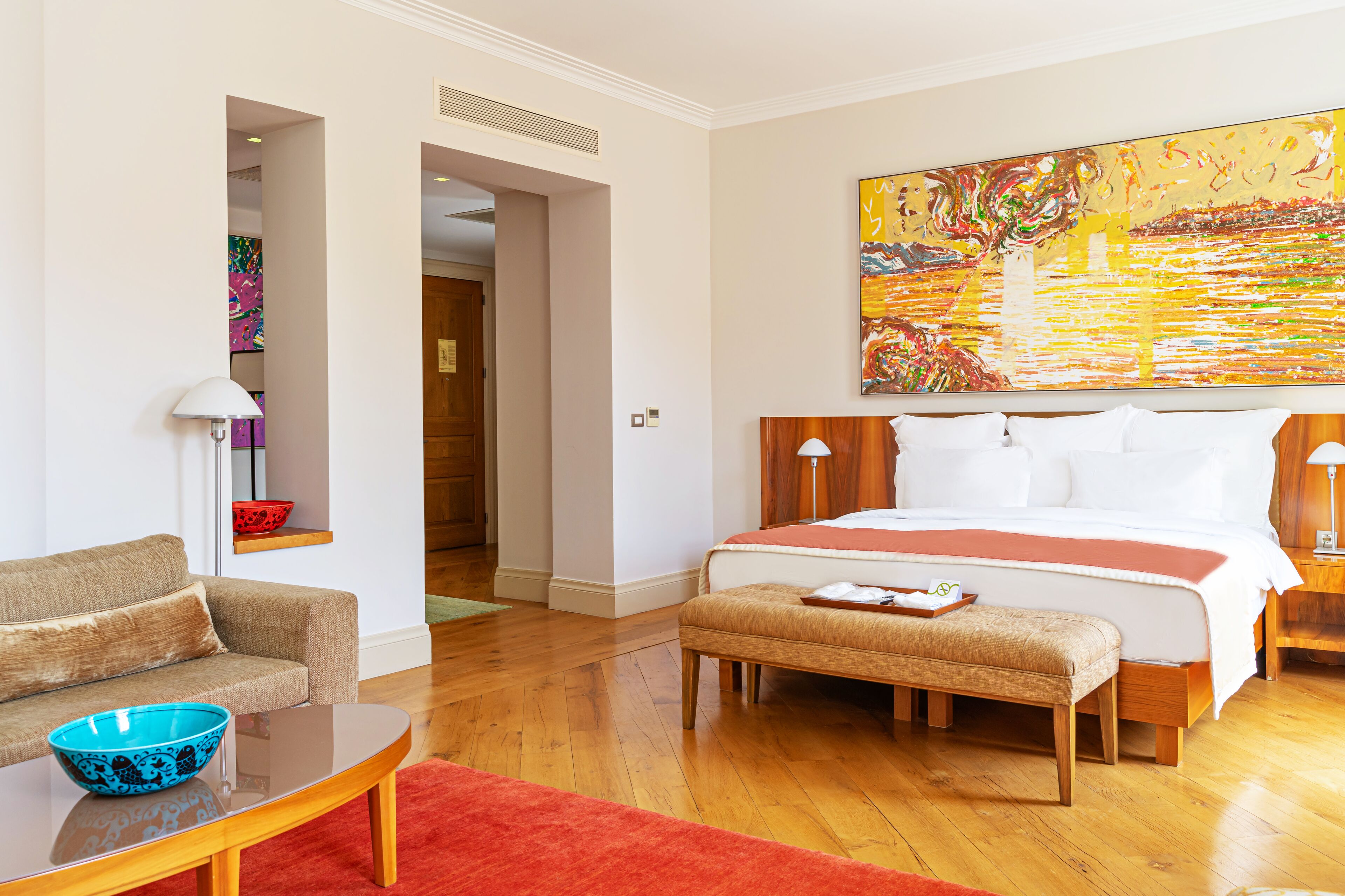 Quarto de hotel com uma cama grande, um sofá, uma mesa de centro e um quadro na parede.