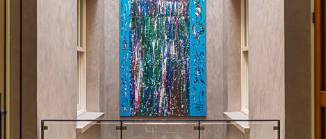 Um átrio amplo com uma grande obra de arte colorida na parede, guarda-corpo de vidro e vista para o interior.