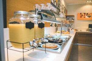 Disposição de buffet com estação de café, diversos doces e seleção de frutas.