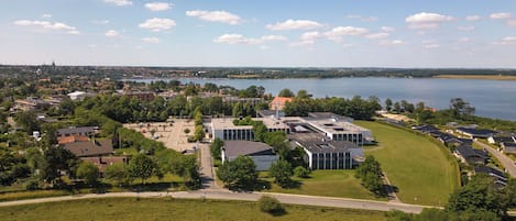 Vista aérea de um campus com edifícios modernos, um grande gramado e um lago ao fundo.