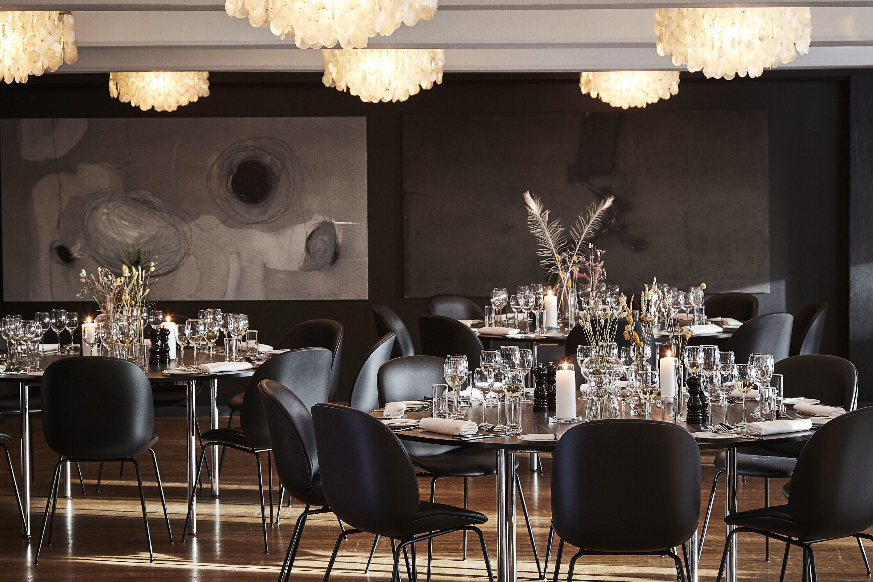 Restaurante com várias mesas preparadas para refeições, com cadeiras pretas, velas e centros de mesa decorativos.