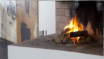 Uma lareira com lenha acesa, uma parede branca com grafites e uma parede de tijolos atrás da lareira.