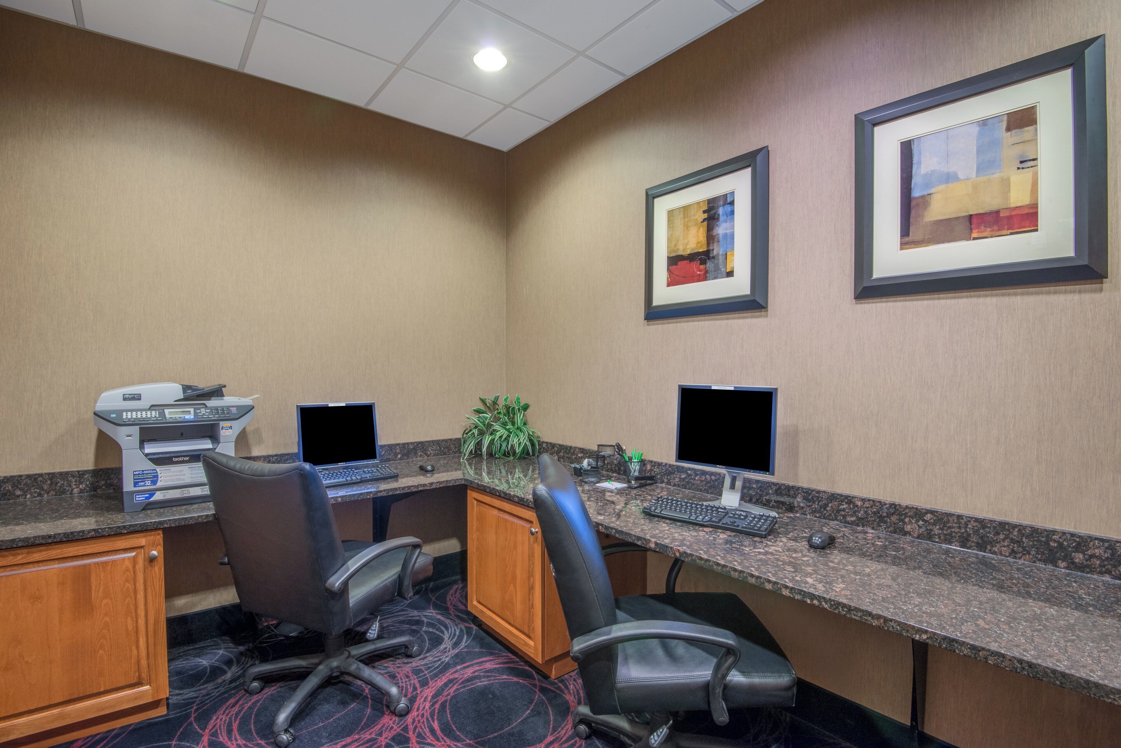 Sala de conferência com duas mesas, cadeiras, uma impressora, dois monitores e quadros nas paredes.