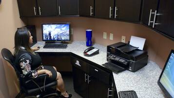 Uma mulher sentada em uma mesa com dois monitores, uma impressora e um teclado.