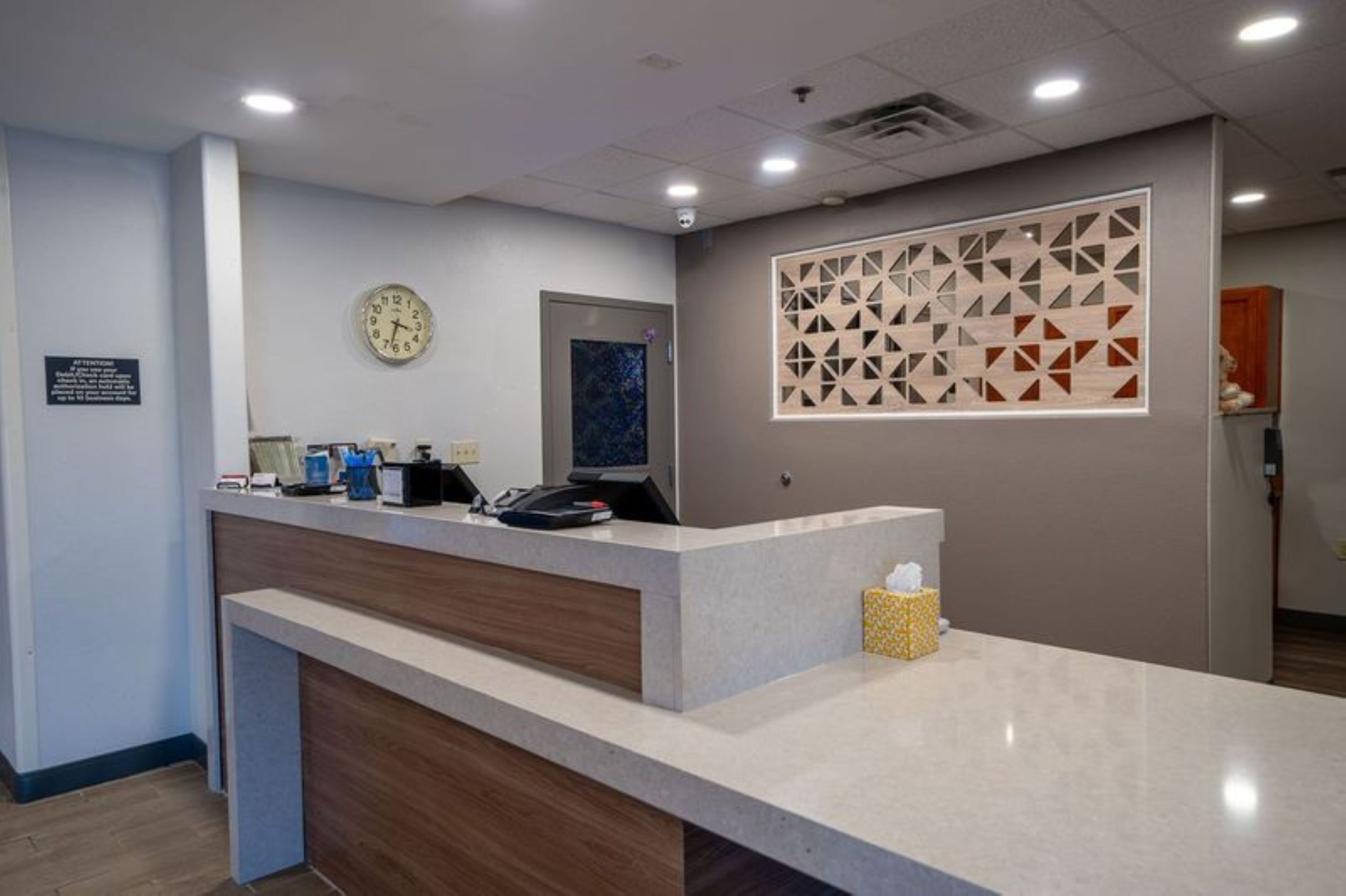 Uma área de recepção com balcão de madeira, um relógio e um painel decorativo.