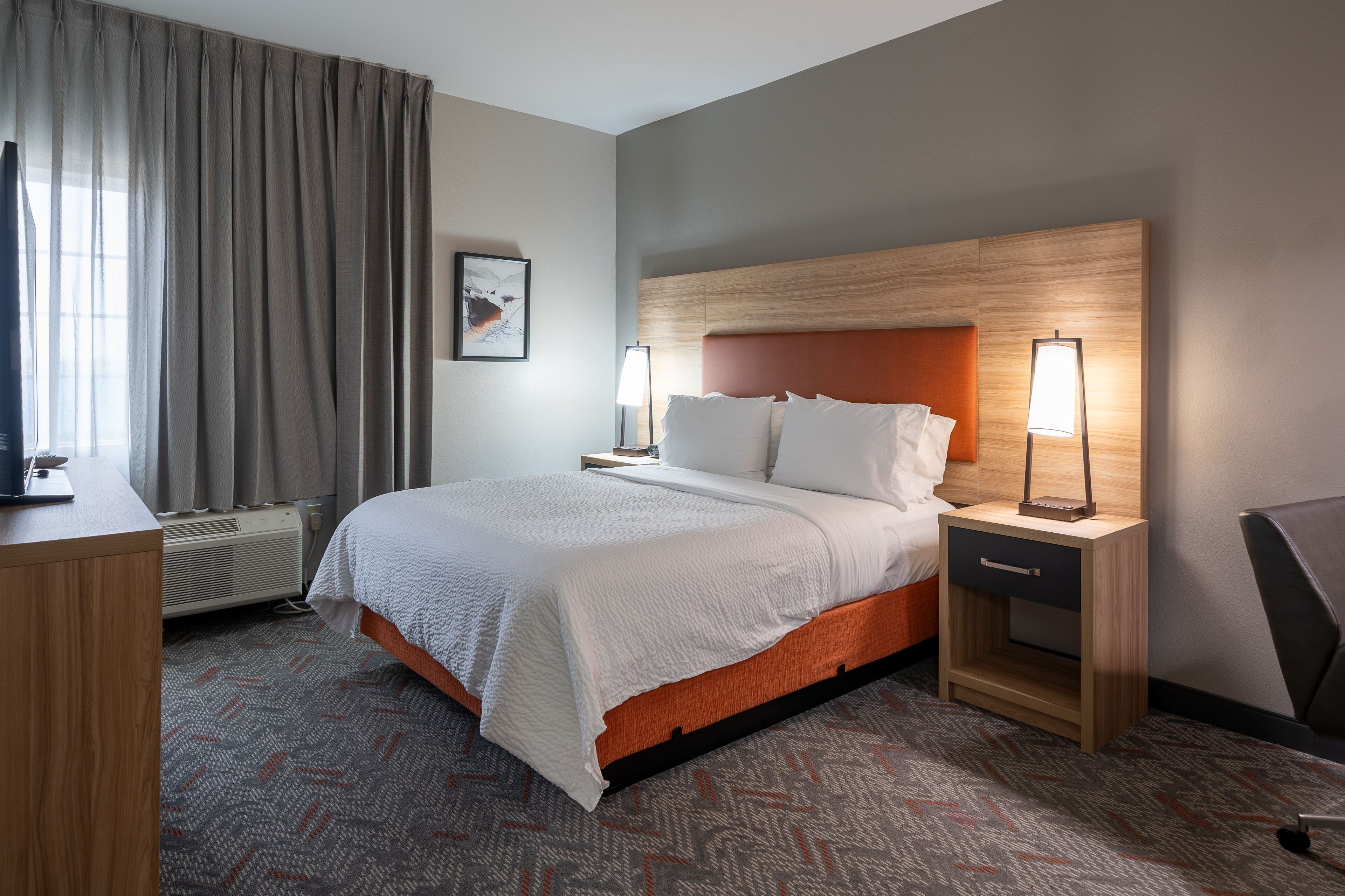 Quarto de hotel com uma cama, duas mesas de cabeceira com luminárias, uma escrivaninha e uma cadeira.