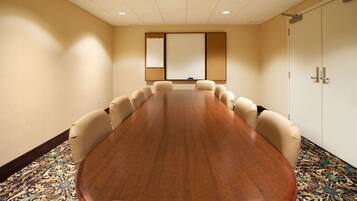 Uma sala de conferência com uma mesa de madeira comprida, rodeada por cadeiras, uma tela de projetor e uma porta com puxador.