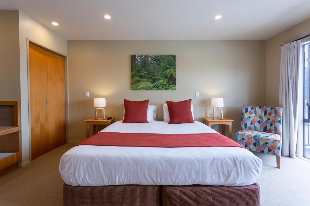 Quarto de hotel com uma cama grande, duas mesas de cabeceira com abajures, uma cadeira colorida, um guarda-roupa e um quadro na parede.