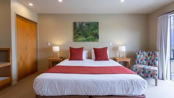 Quarto de hotel com uma cama grande, duas mesas de cabeceira com abajures, uma cadeira colorida, um guarda-roupa e um quadro na parede.