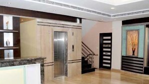 Um hall amplo com uma receção em mármore, uma escadaria e uma obra de arte emoldurada na parede.
