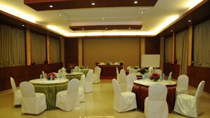 Uma sala de conferência com mesas redondas, cadeiras brancas e centros de mesa com flores.