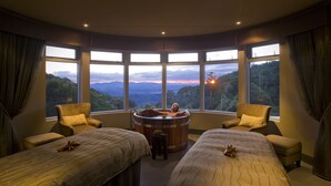 Quarto com duas camas, banheira e amplas janelas com vista para as montanhas.