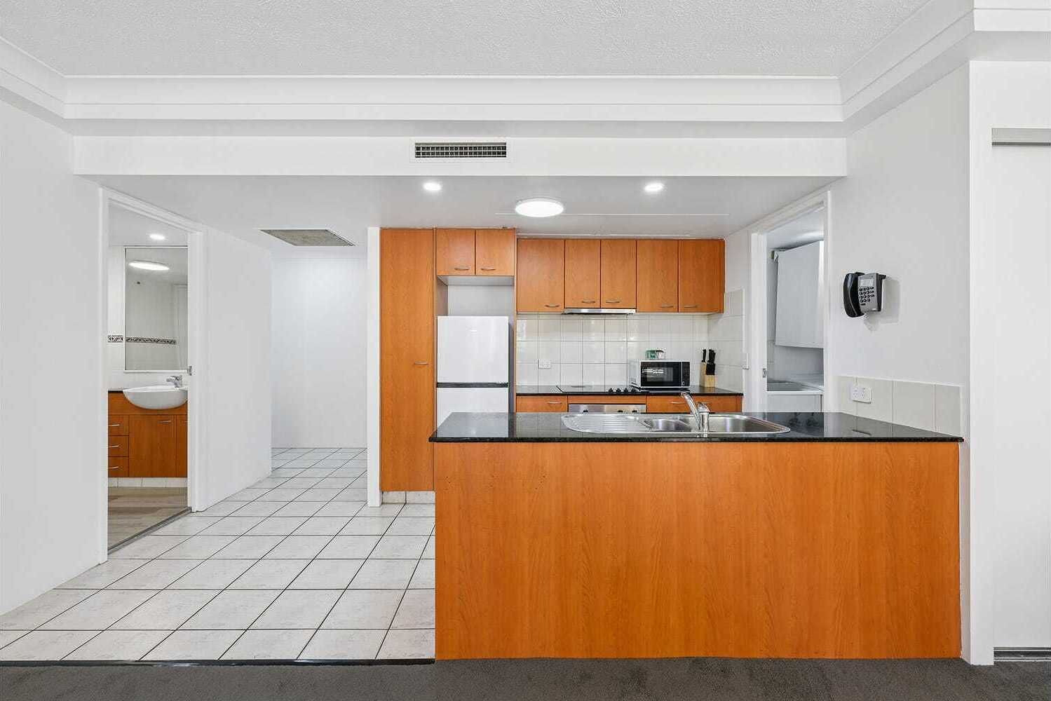 Uma cozinha moderna com armários de madeira, uma pia de aço inoxidável e micro-ondas embutido.