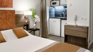 Quarto de hotel com cama, uma pequena escrivaninha, mesa de cabeceira, luminária, um vaso com flores, micro-ondas e telefone.