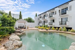 Uma área de piscina com um gazebo, cercada por um prédio branco com varandas.
