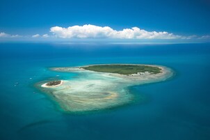 Vista aérea de uma ilha tropical com águas turquesa cristalinas, uma pequena praia e alguns barcos.