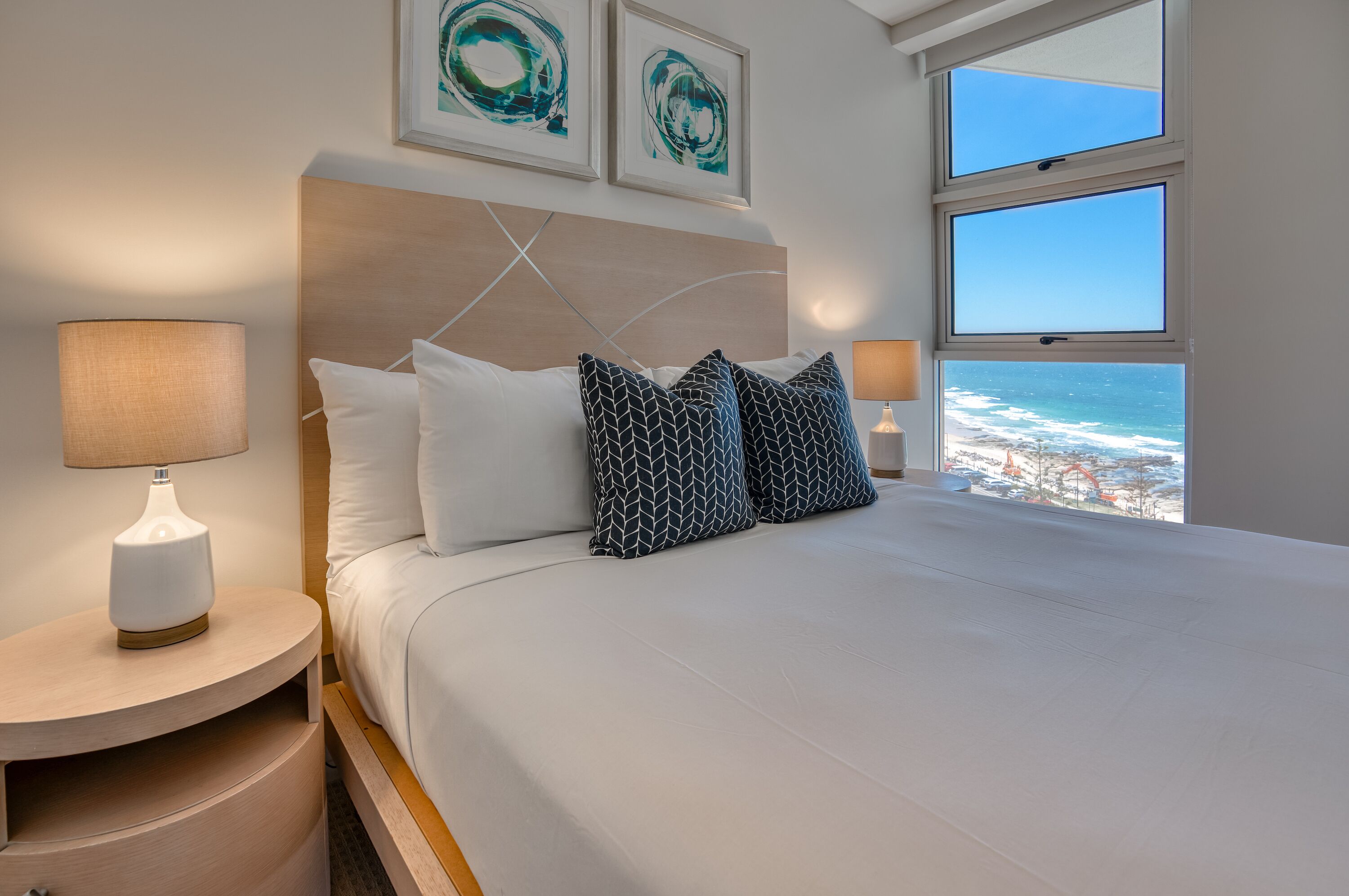 Quarto com uma cama, duas mesas de cabeceira, um encosto e vista para o oceano através de grandes janelas.