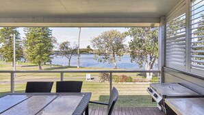 Área externa coberta com mesa, cadeiras, churrasqueira e vista para um lago e árvores.