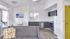 Cozinha moderna com armários brancos, lava-louças e fogão. Há uma área de jantar com mesa e cadeiras.