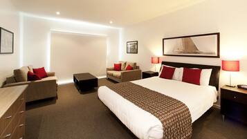 Quarto de hotel com uma cama grande, duas poltronas, uma mesinha e uma escrivaninha.