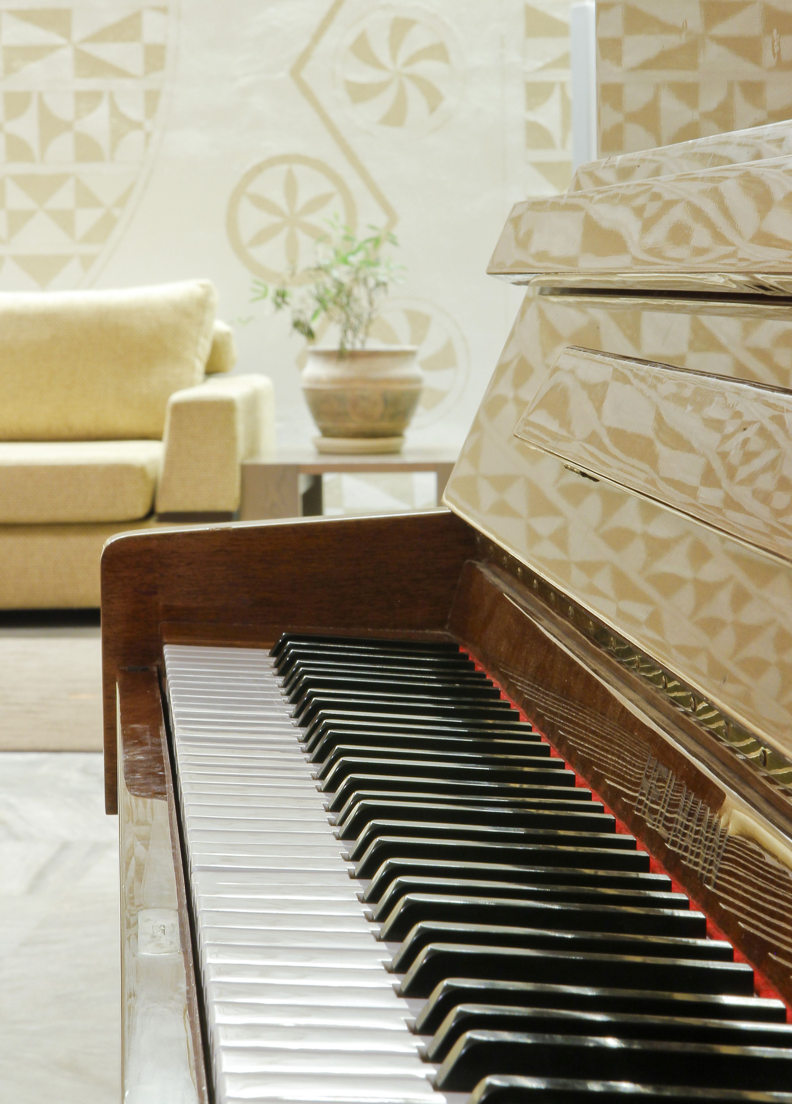 Um piano numa sala com parede estampada e um sofá ao fundo.