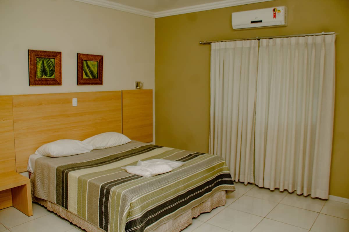 Uma cama bem arrumada com colcha listrada, cabeceira de madeira e duas molduras com quadros na parede.