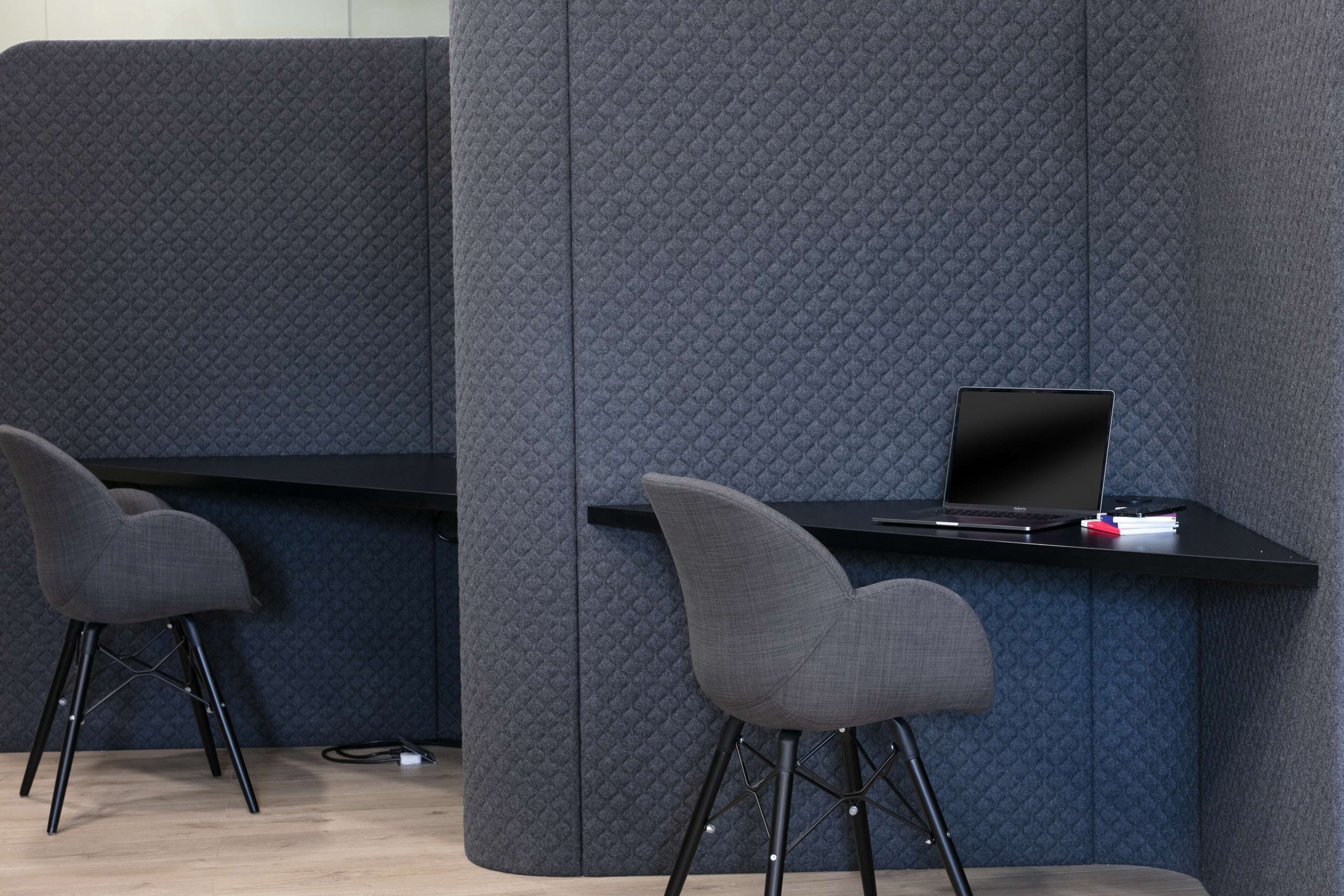 Um espaço de escritório moderno com uma mesa preta, duas cadeiras cinzas e um laptop.