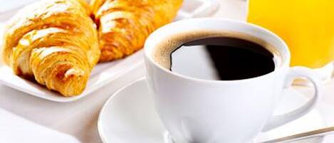 Uma mesa de café da manhã com croissants, uma xícara de café e um copo de suco de laranja.