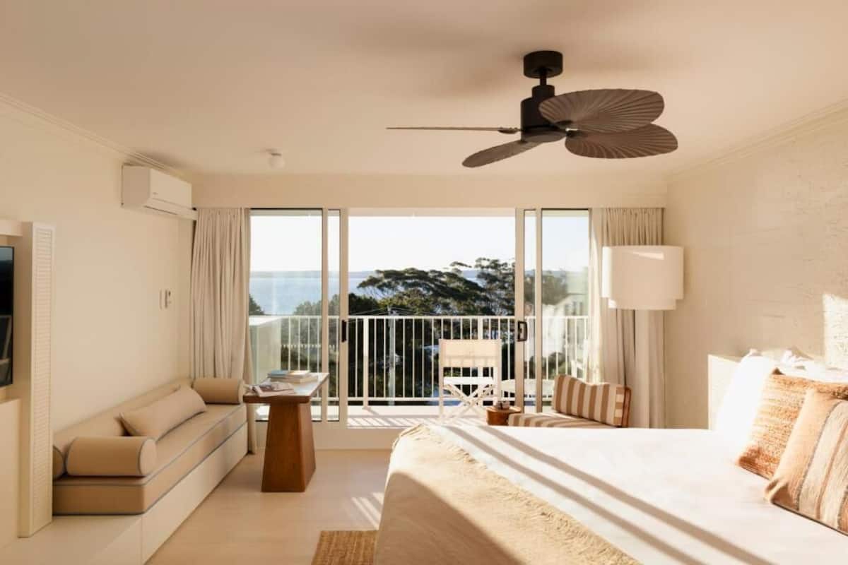 Quarto de hotel com cama grande, sofá, mesa pequena e varanda vista para o mar.