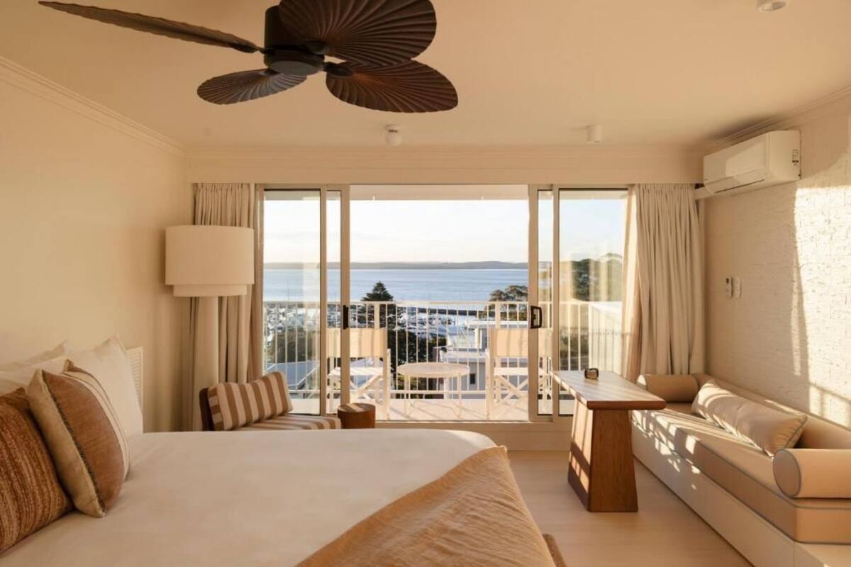 Quarto de hotel com cama grande, varanda vista para o mar, ventilador de teto e sofá.