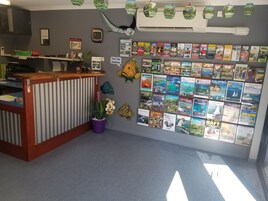 Uma área de recepção com balcão de madeira, um relógio, ar-condicionado fixado na parede e uma parede com folhetos de viagens.