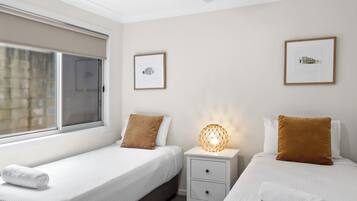 Quarto de hotel com duas camas de solteiro, ventoinha no teto, janela com persianas e dois quadros na parede.
