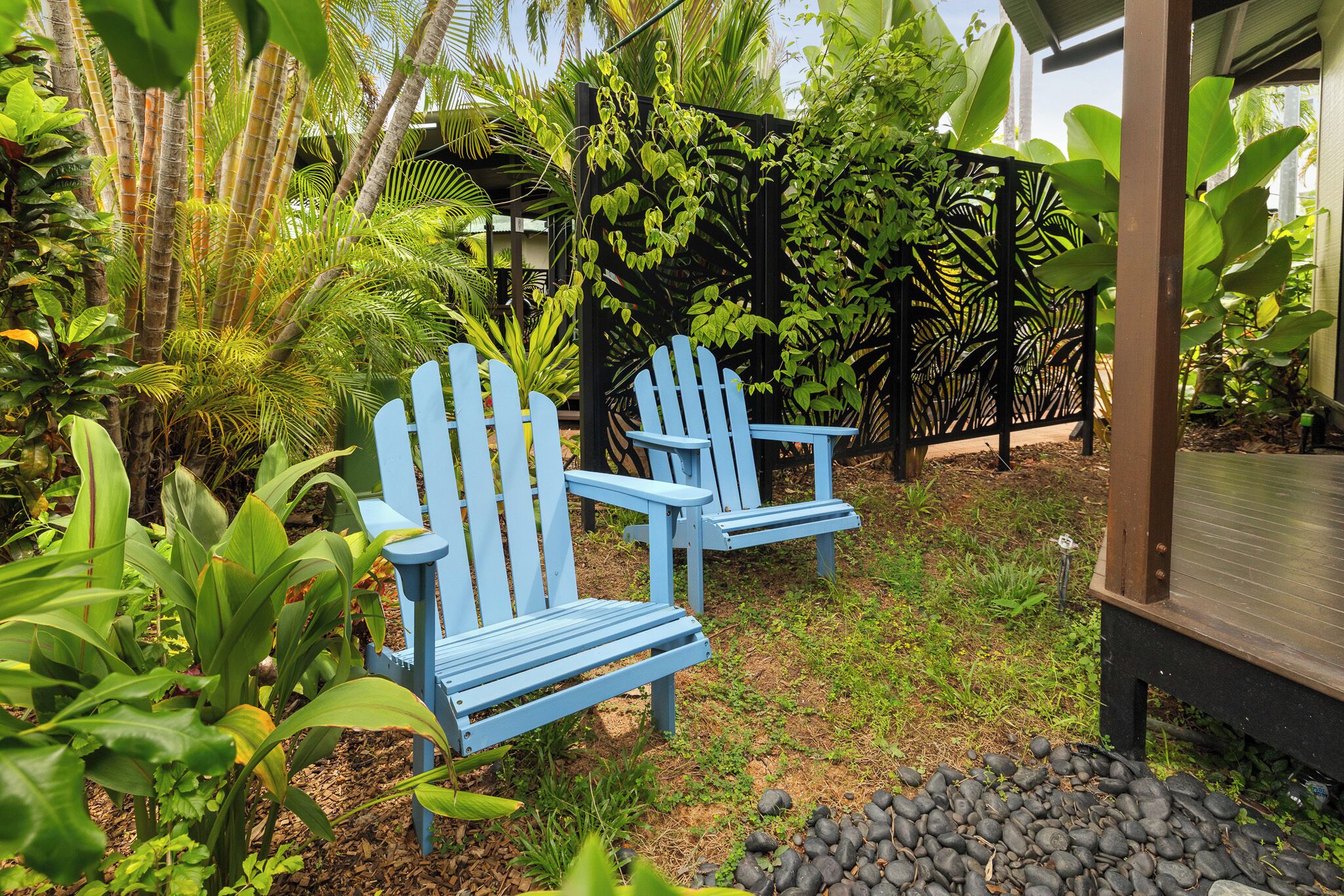 Duas cadeiras Adirondack azuis num jardim com plantas tropicais e um deck de madeira.