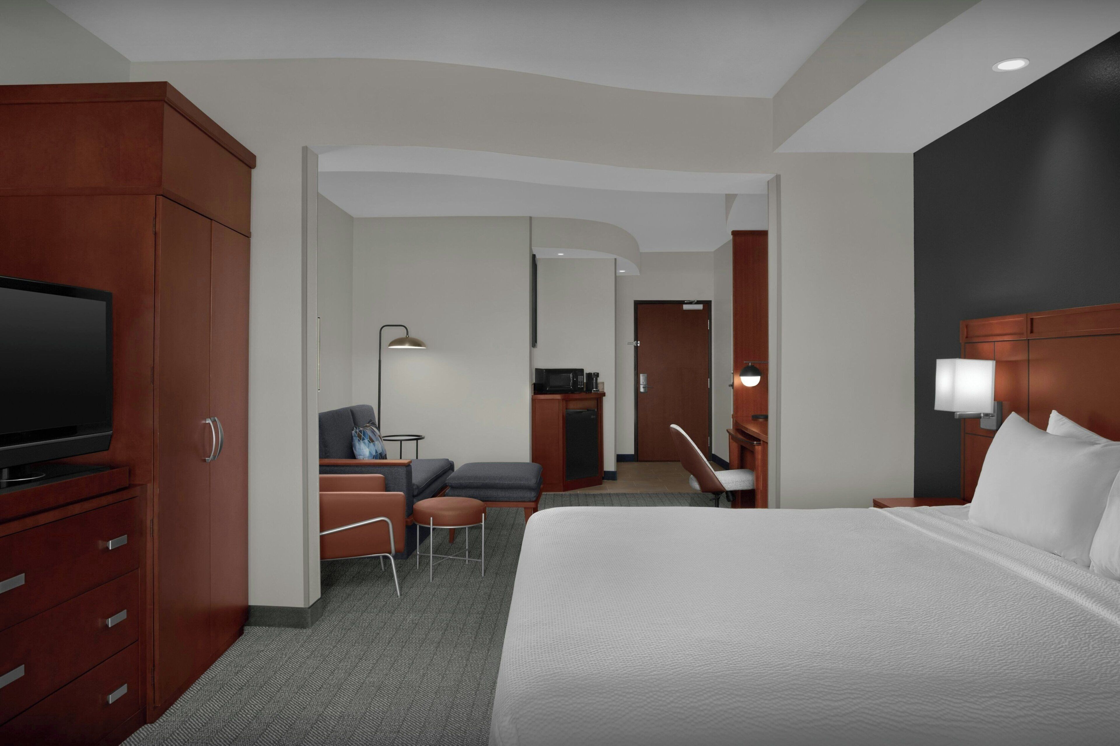Quarto de hotel com uma cama grande, televisão, escrivaninha com cadeira, mesinha e sofá.
