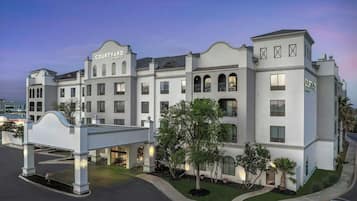 Um hotel de vários andares com design arquitetônico moderno, com entrada destacada e galeria coberta, além de paisagismo bem cuidado.