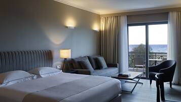 Quarto de hotel com duas camas, um sofá, uma cadeira, um abajur e varanda com vista para o mar.