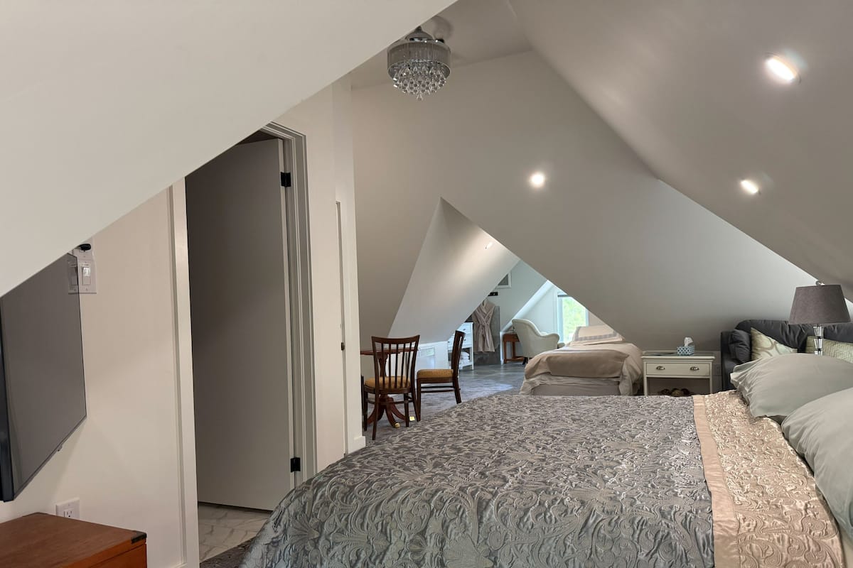 Quarto no sótão com uma cama grande, um lustre e vista para o quarto vizinho.