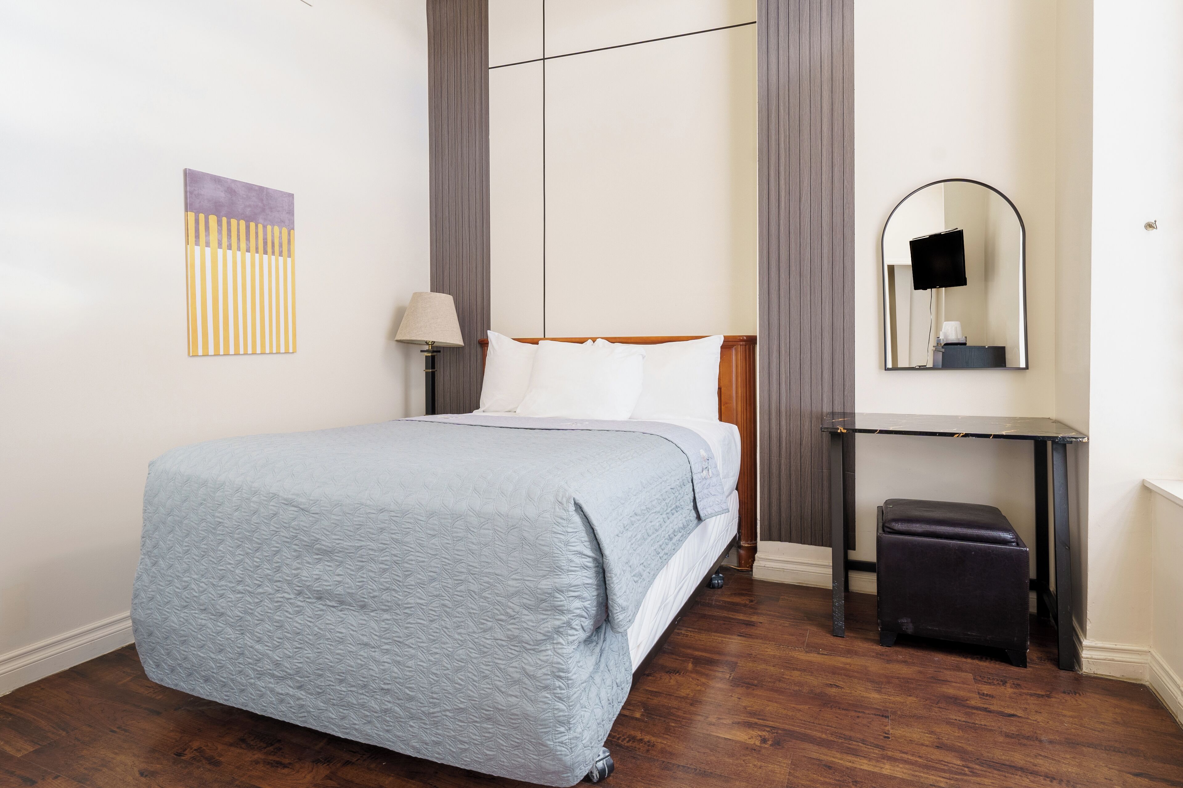 Quarto de hotel com cama, escrivaninha, espelho e um pequeno banco.