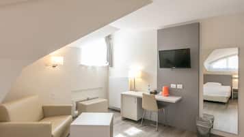 Quarto de hotel moderno com sofá, escrivaninha, cadeira, televisão e cama com dossel.