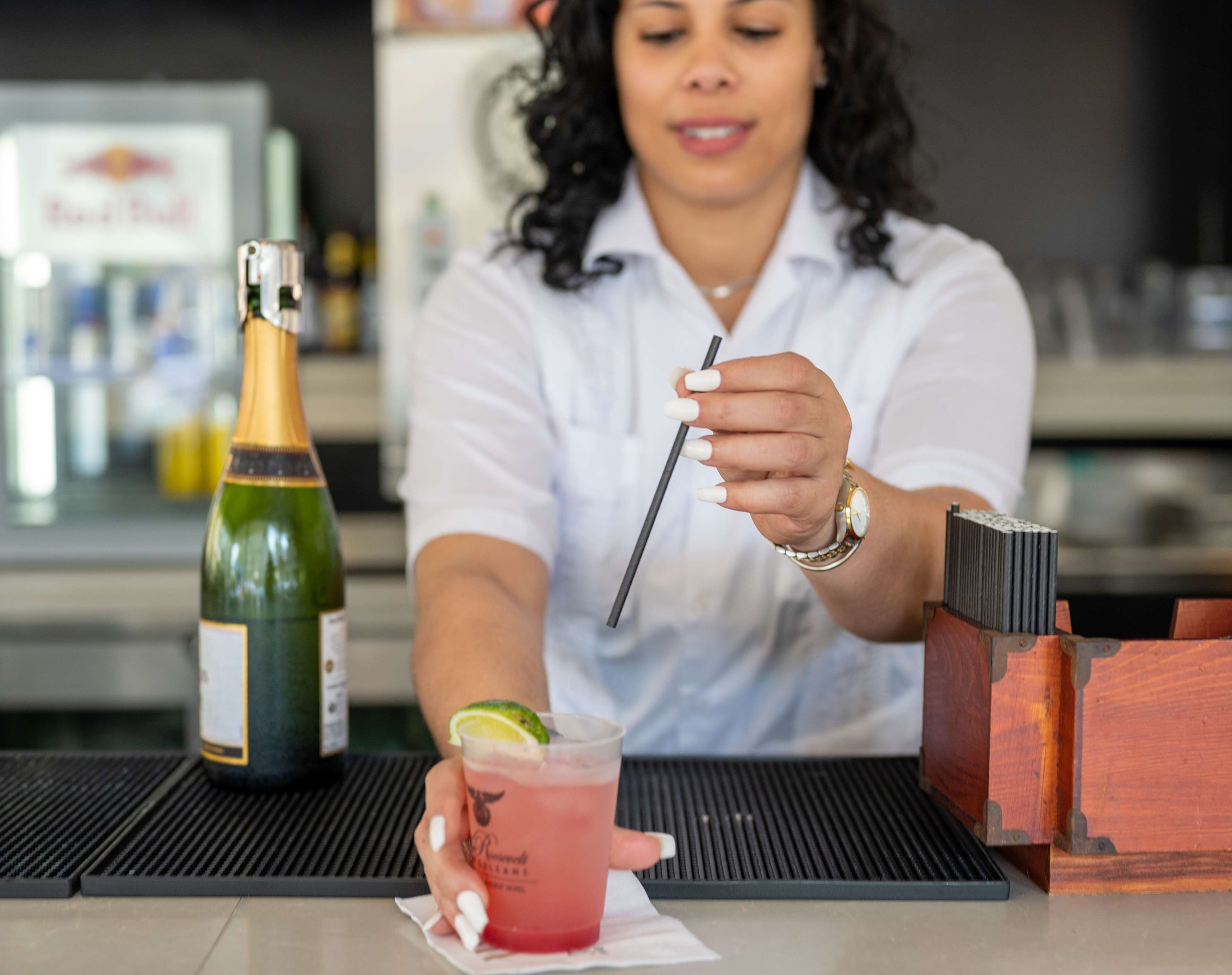 Um bartender preparando uma bebida com uma garrafa de champanhe e um copo de coquetel sobre um apoio de bar.